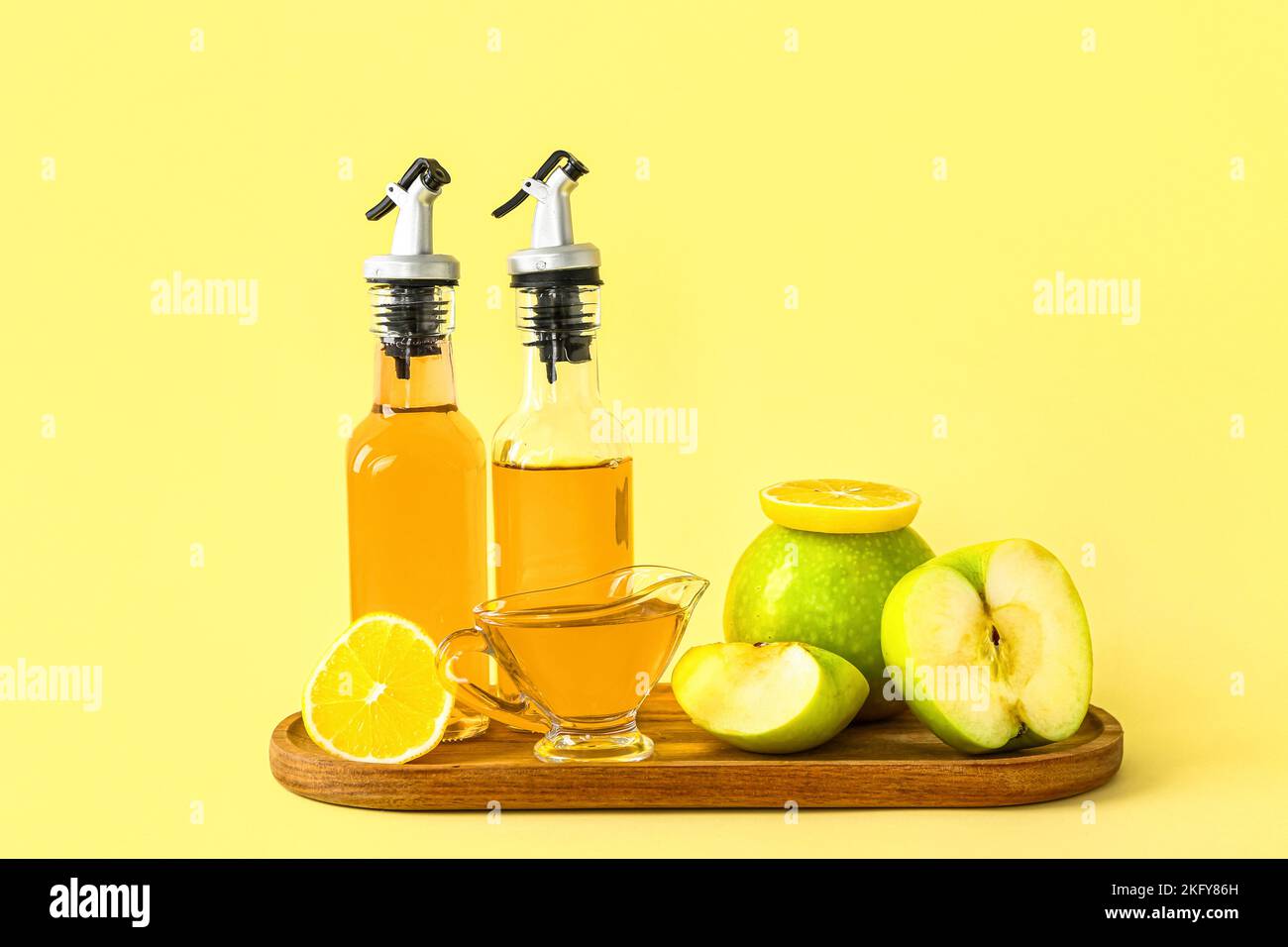 Wooden board with bottles of apple cider vinegar and fruits on yellow ...