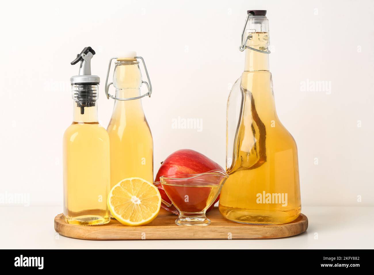 Wooden board with bottles of apple cider vinegar and fruits on light ...