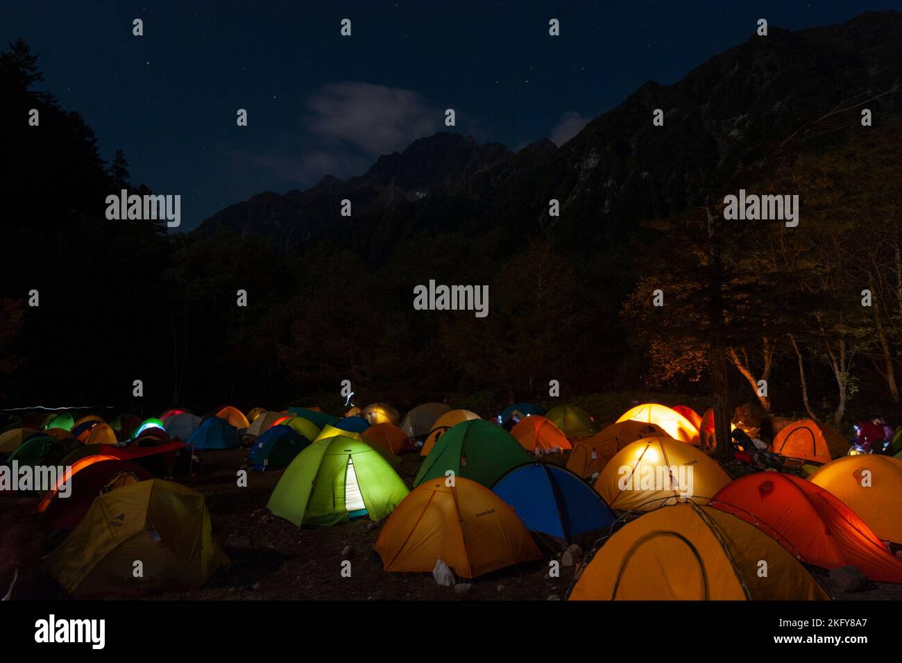 Tents lit up at night, below the peaks of the Japan Alps, on a busy ...