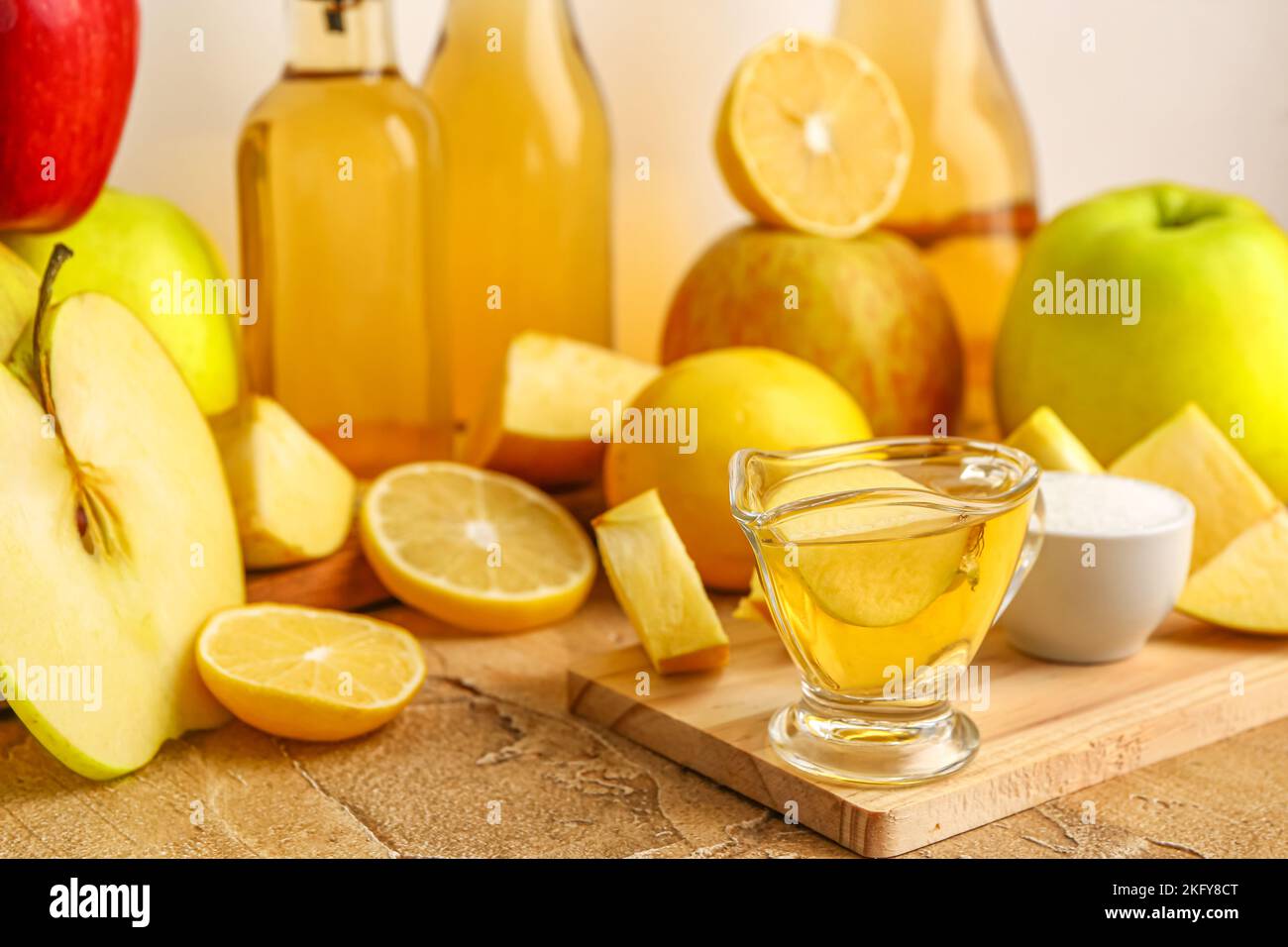 Wooden board with gravy boat of apple cider vinegar and fruits on color ...