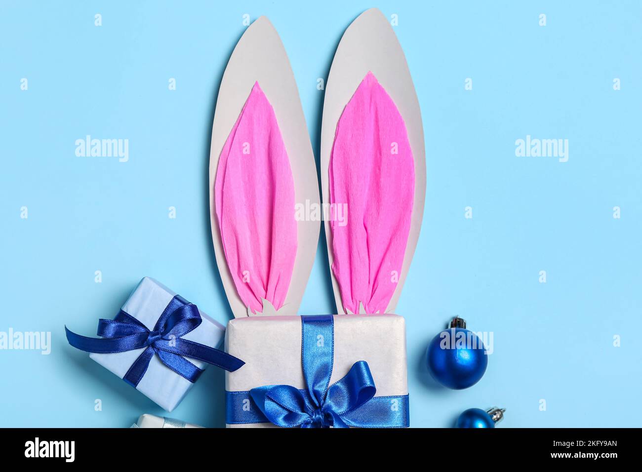 Paper bunny ears with Christmas balls and gifts on blue background ...