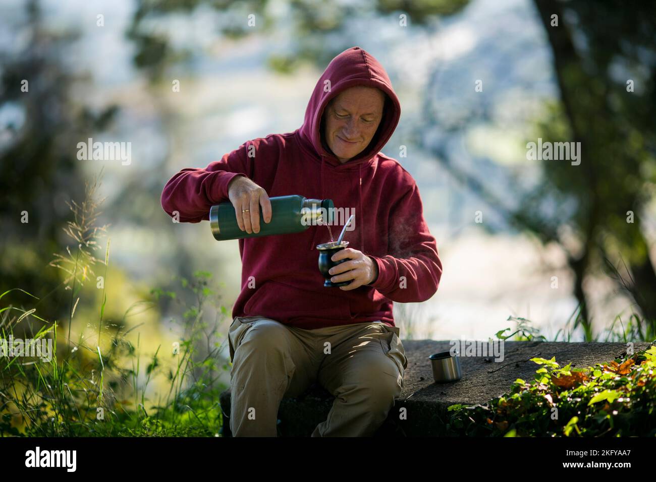 A man in the park pours boiling water from a thermos into a Mate cup ...