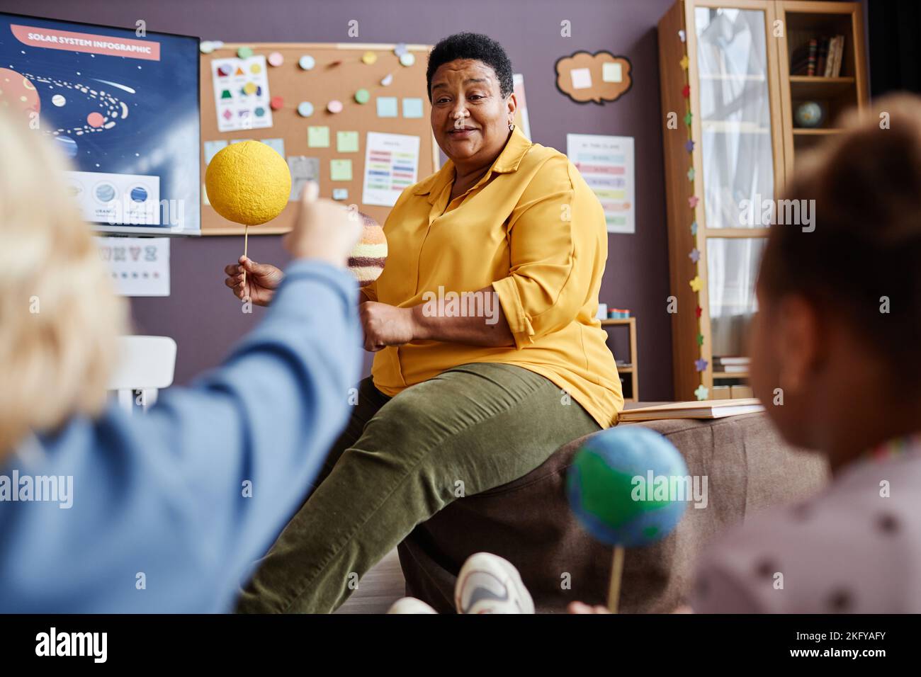 Focus on mature teacher with planet of sun interacting with little ...