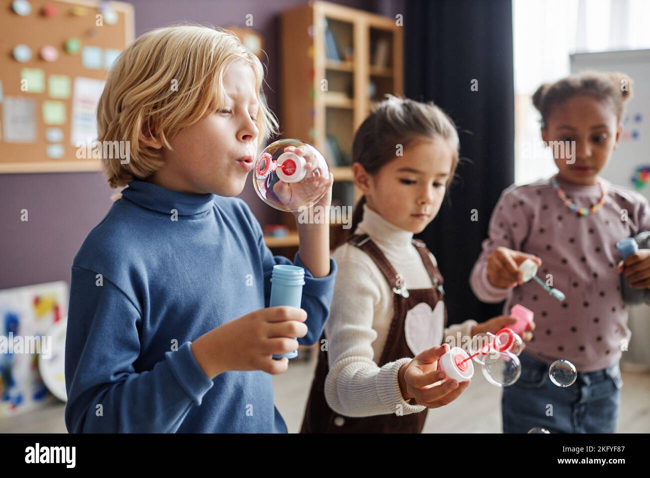 Cute blond boy blowing soap bubbles in front of camera against two ...