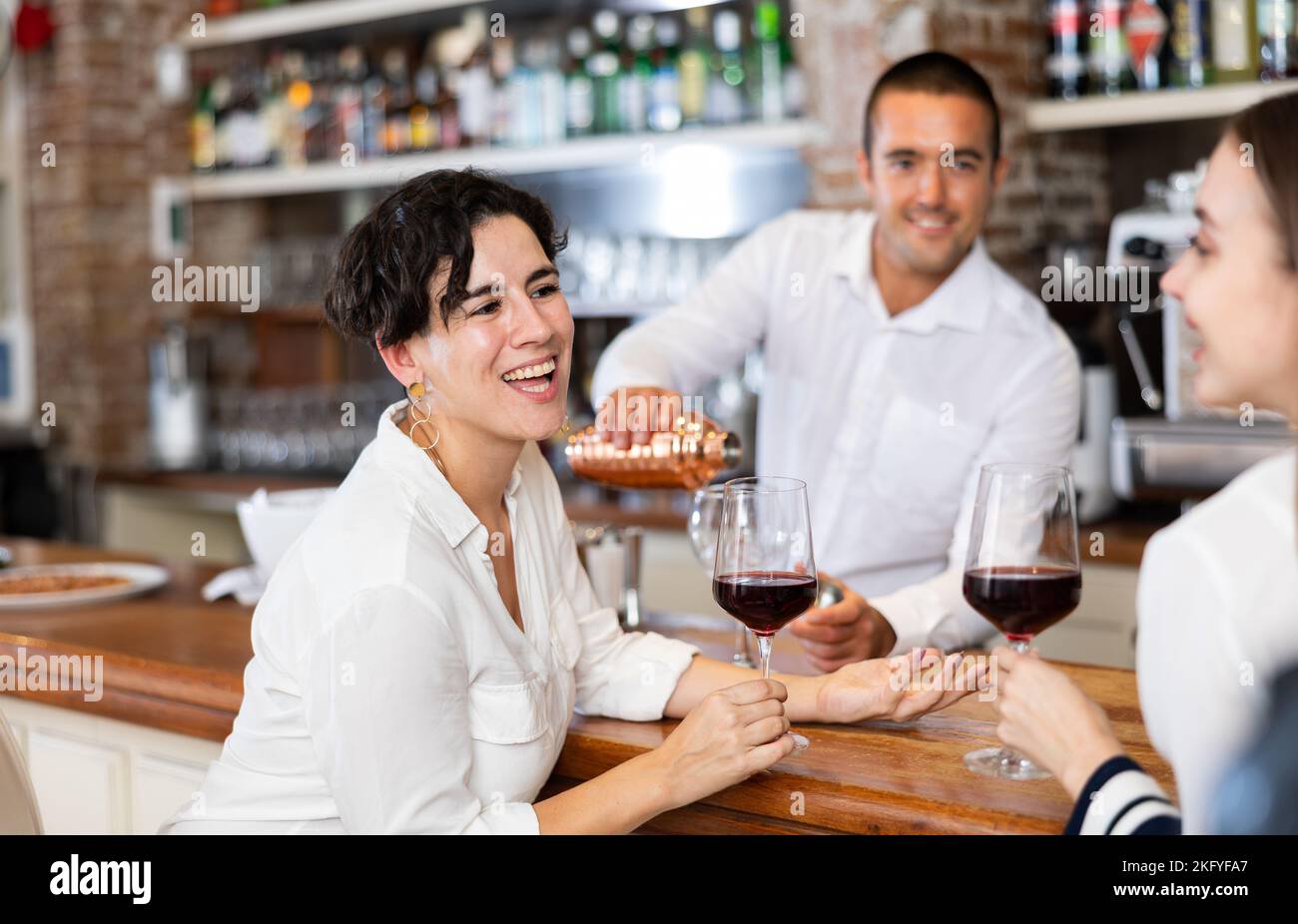 Two girlfriends chat with each other and drink red wine while sitting ...