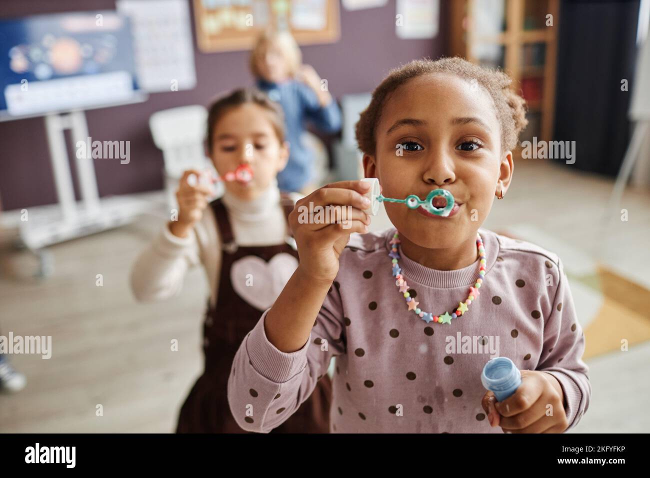 Adorable little girl blowing soap bubble while having fun in front of ...
