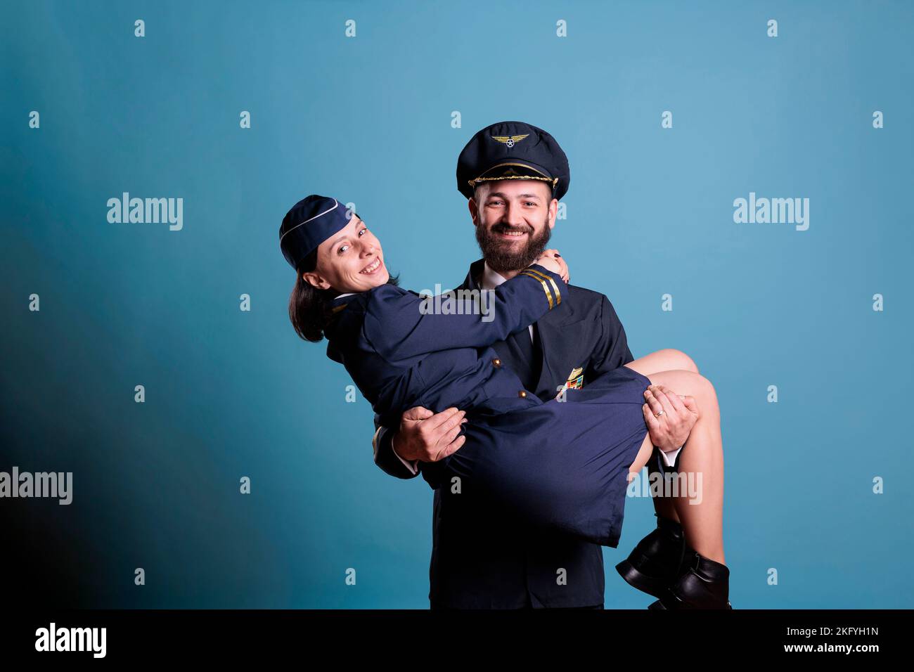 Smiling pilot holding flight attendant in arms portrait, aircrew in ...