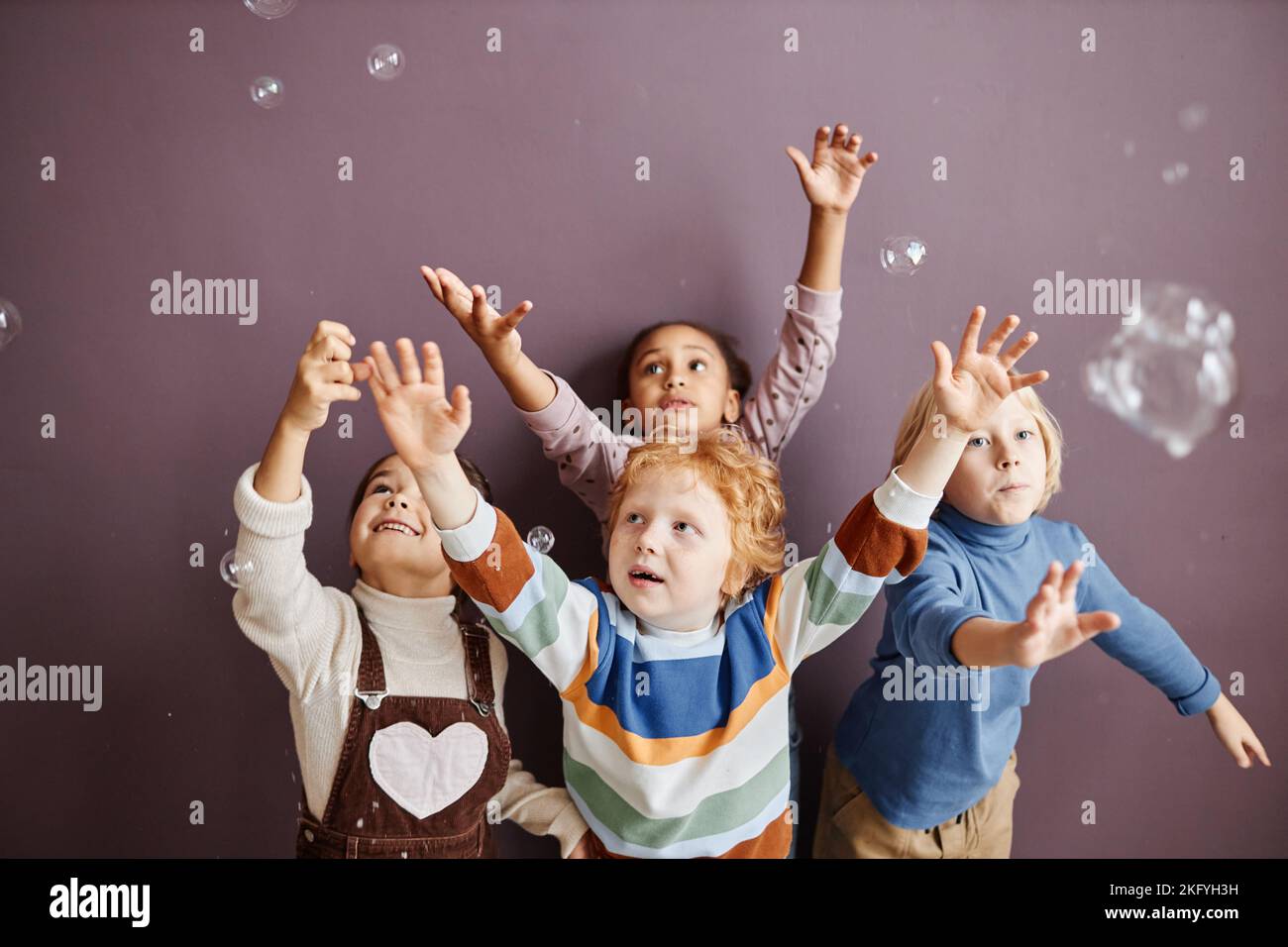 Group of cheerful cute little children in casualwear raising their ...