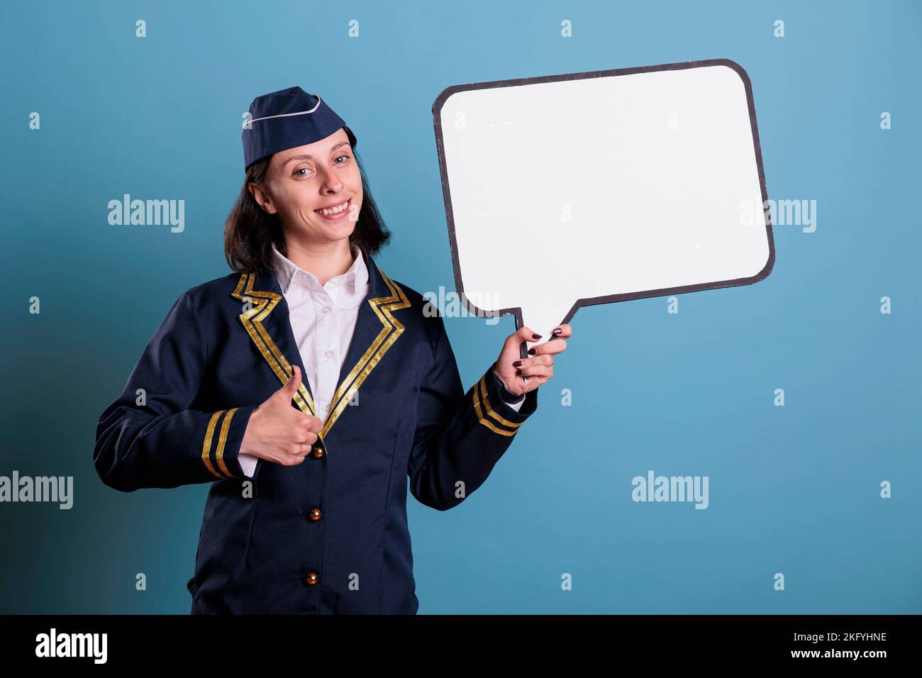 Smiling flight attendant holding white blank speech bubble, showing ...