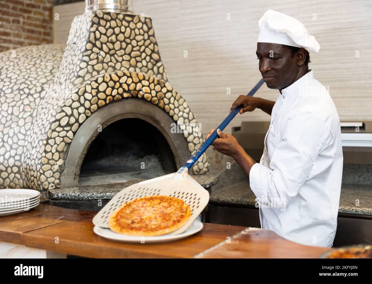 Positive man chef preparing pizza in pizzeria Stock Photo - Alamy