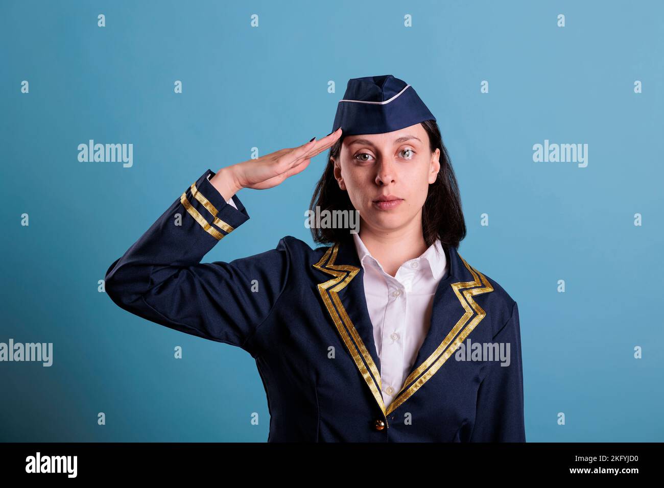 Young serious stewardess saluting, wearing flight uniform, standing ...