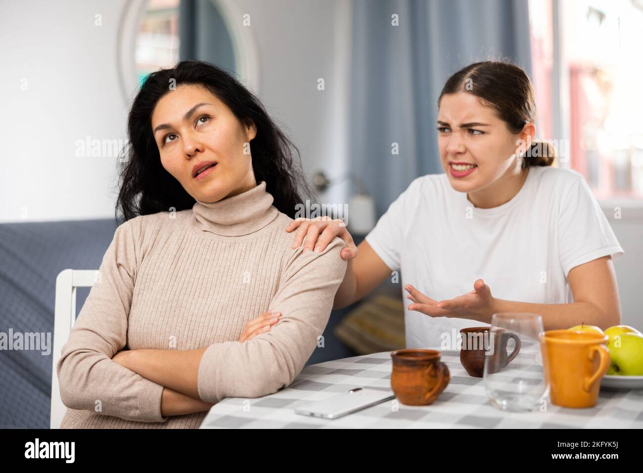 Upset woman sitting at home table with disgruntled woman behind Stock ...