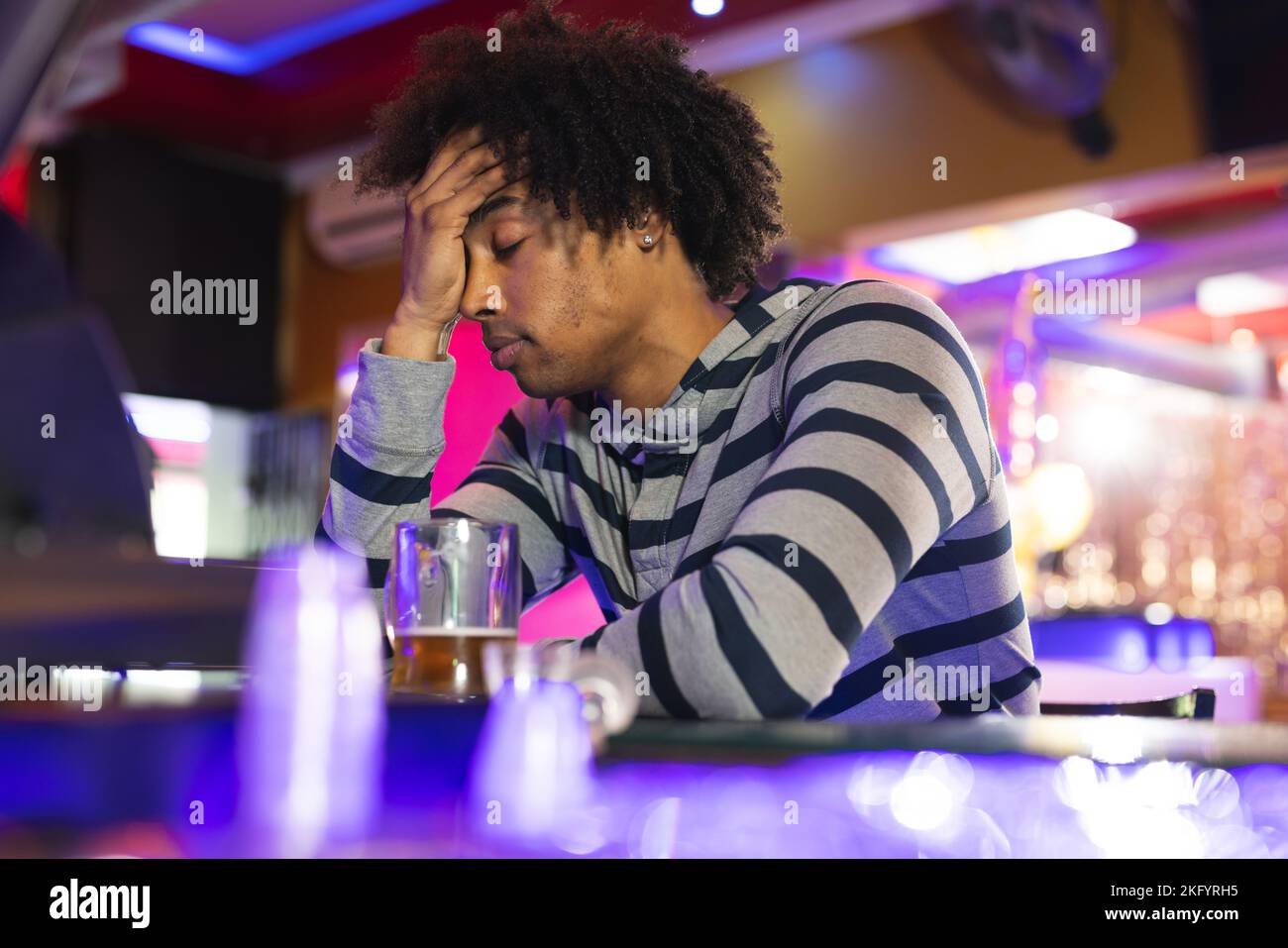 Drunk african american man holding his head sitting at the bar with a ...