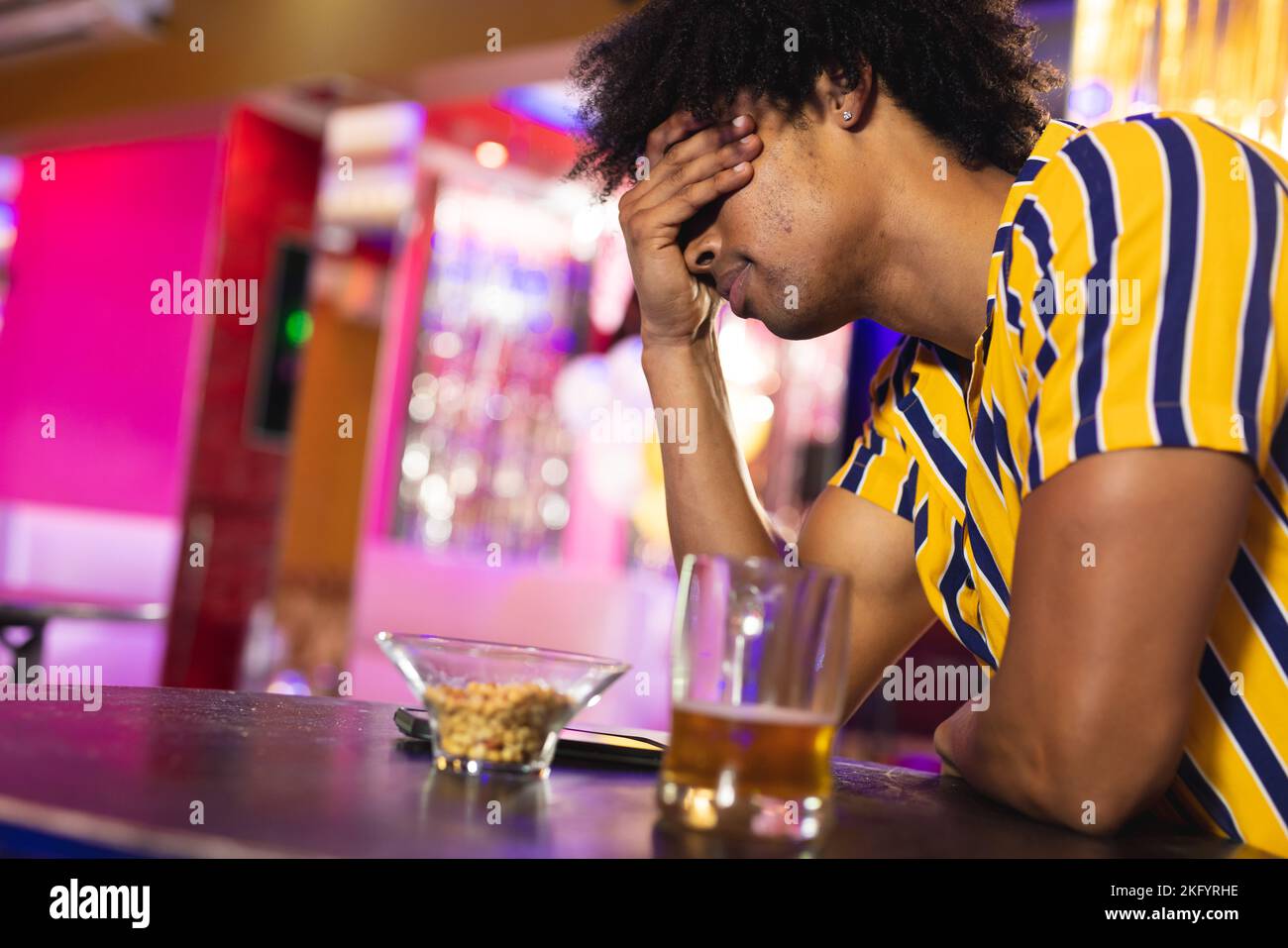 Depressed african american man sitting at the bar with a beer and ...