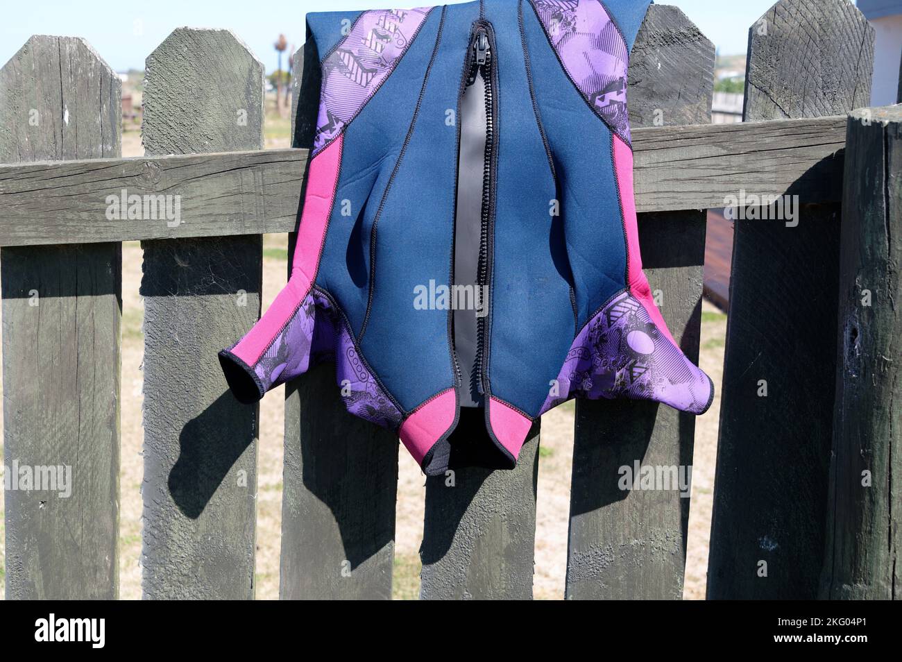 A wetsuite has been thrown over a fence to dry out. It is a shorty ...