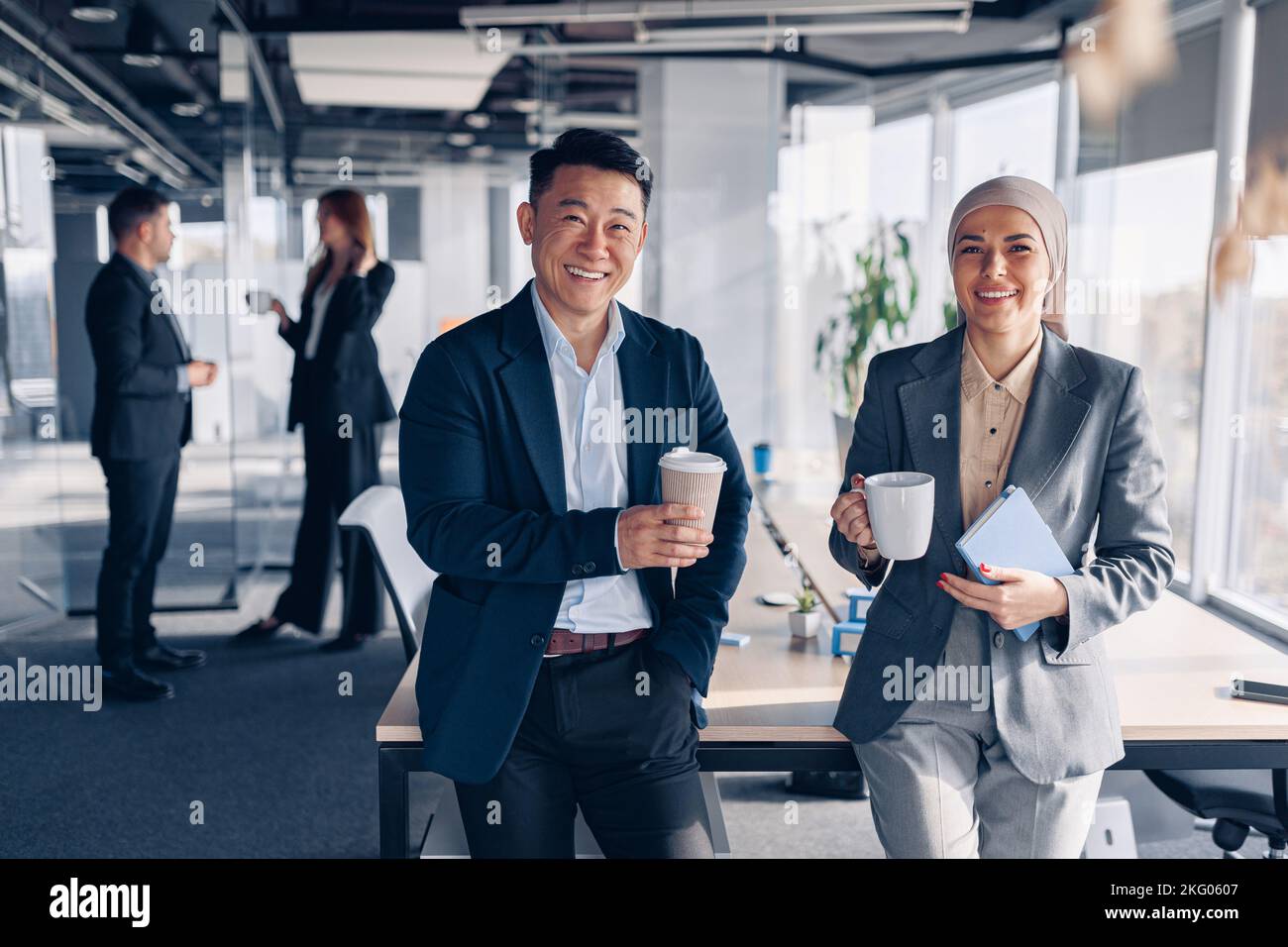 Two happy multiracial colleagues talking and drinking coffee during ...