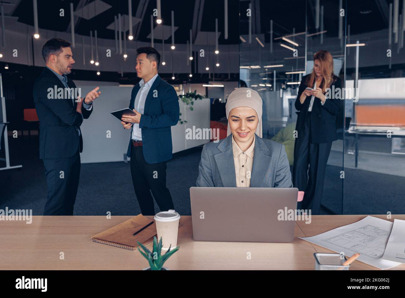 Smiling muslim businesswoman in hijab working on computer while sitting ...