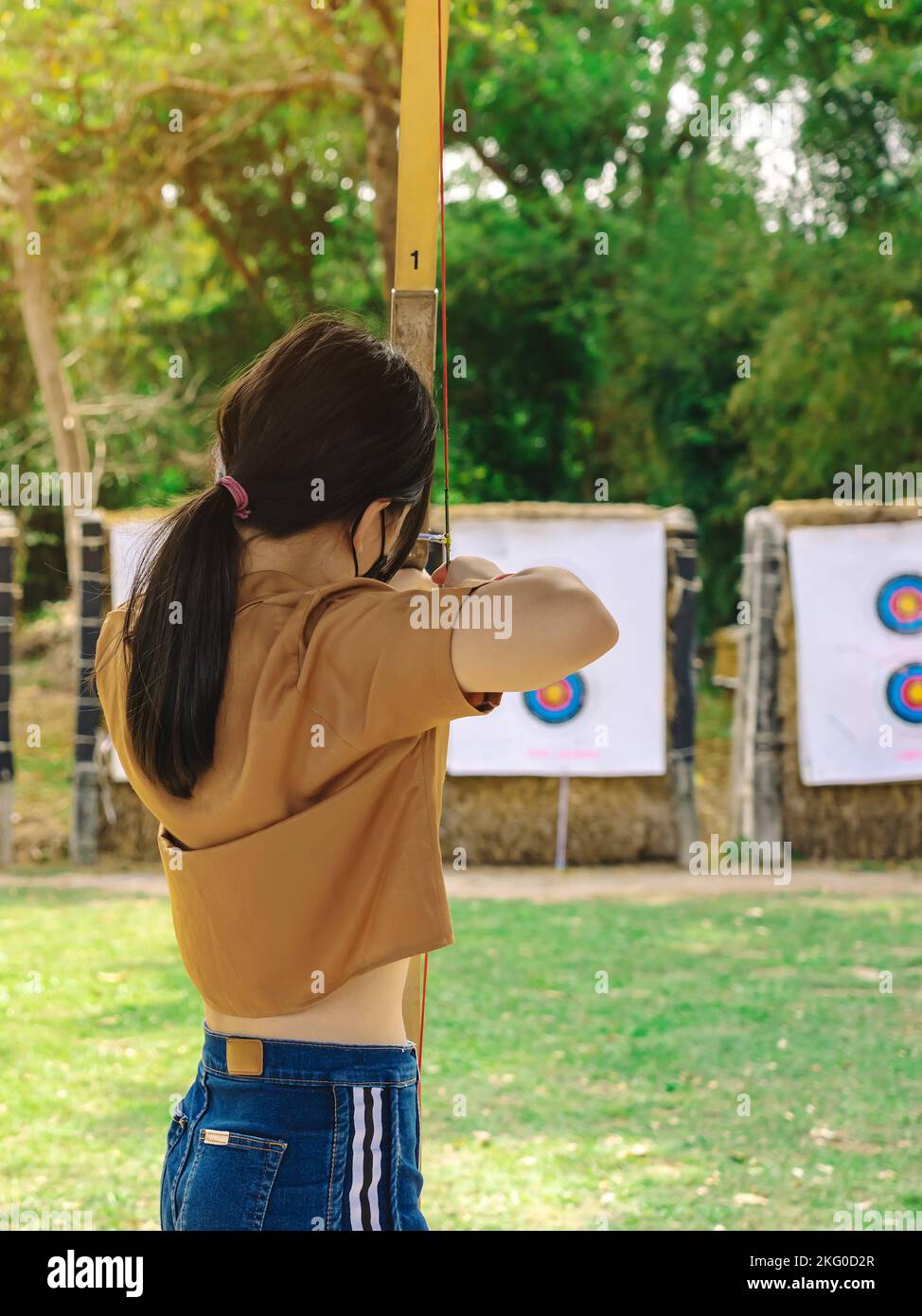 Back view of Asian girl wear face mask aims archery bow and arrow to ...
