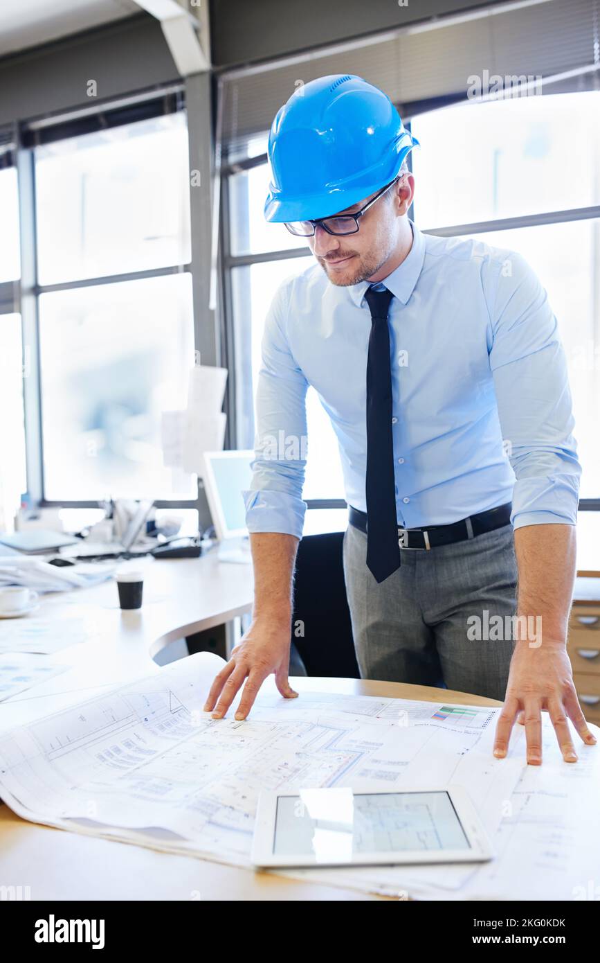 Fine tuning his design. an architect wearing a safety helmet and examining blueprints Stock ...