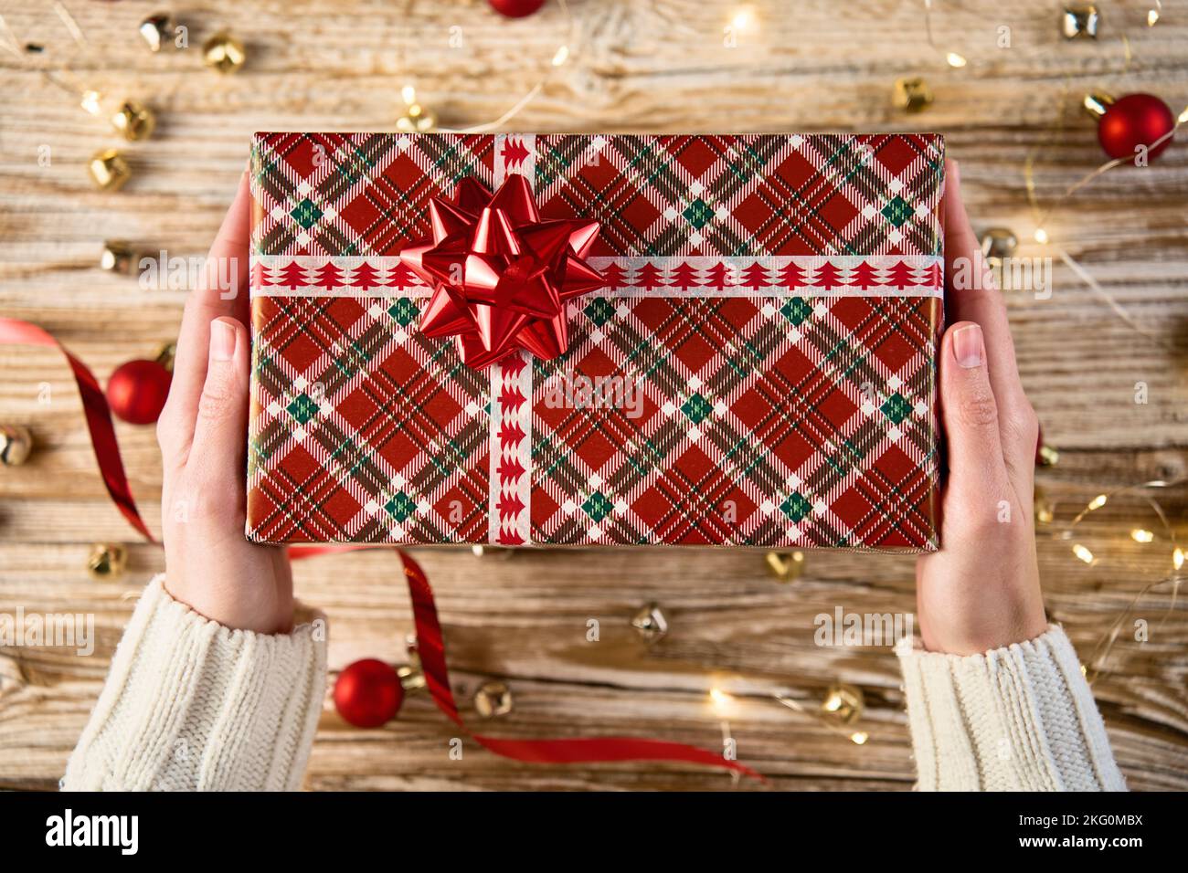 Woman holds gift box wrapped in craft paper with festive ribbon agains ...