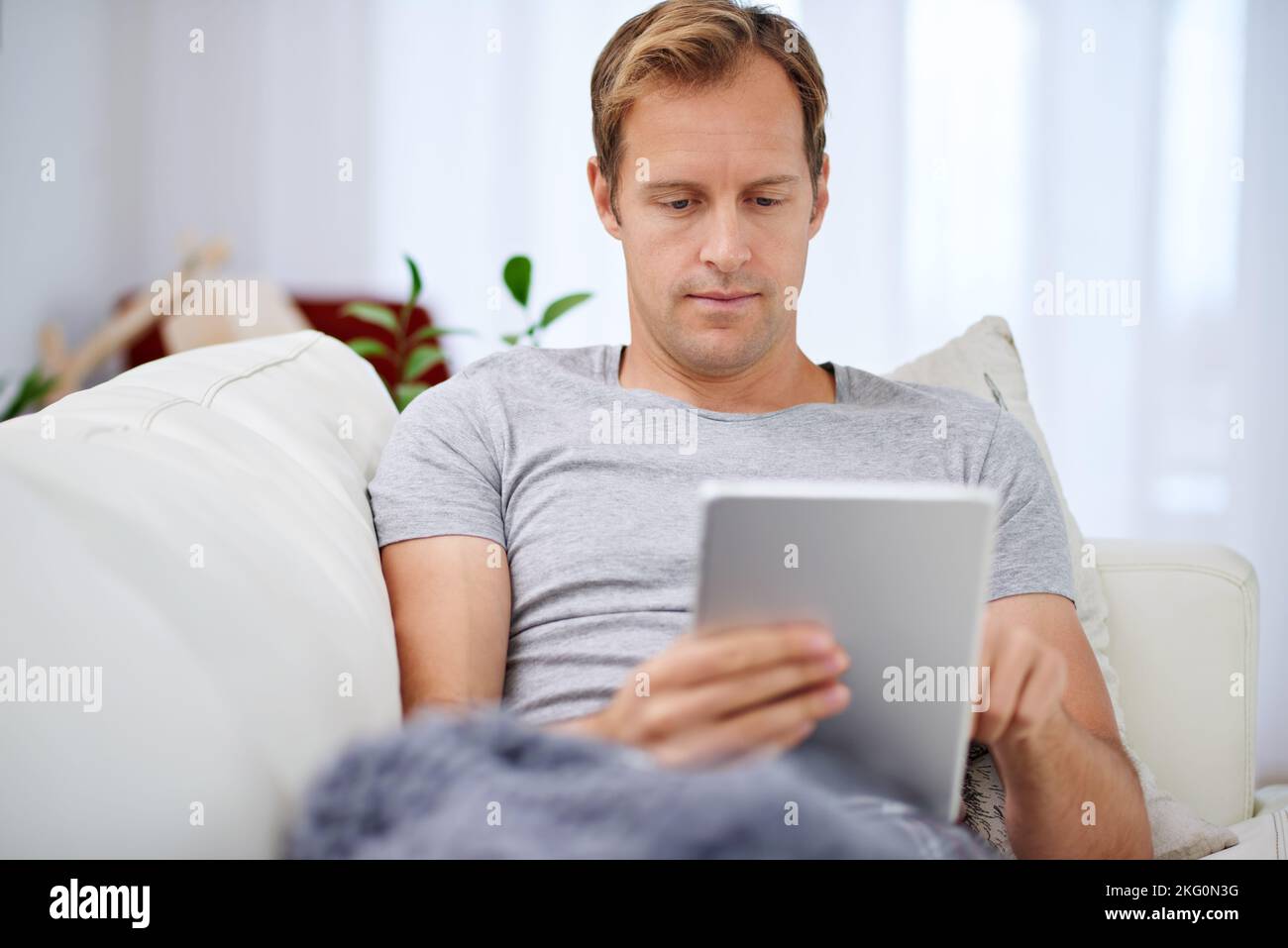 Chilling on the sofa with his tech. a handsome man relaxing with his ...