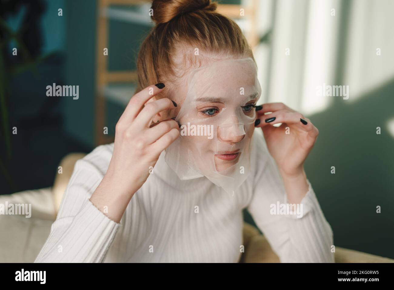 Beautiful young caucasian ginger woman applying paper sheet mask on her ...