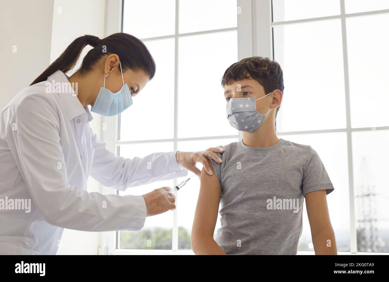 Doctor is giving a vaccine injection to teen boy in shoulder in clinic ...