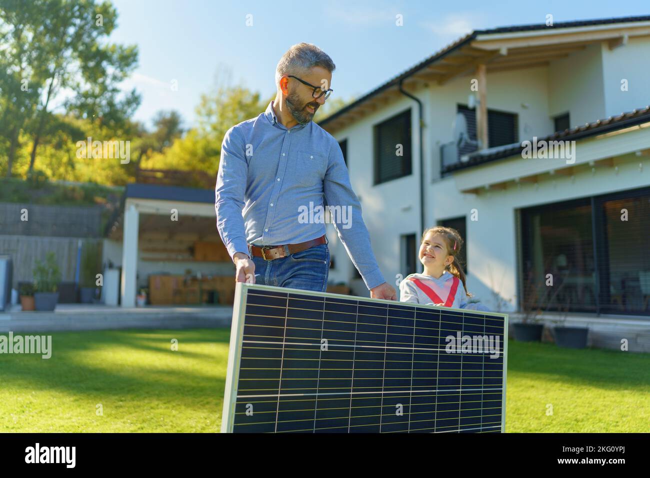 Father with his little daughter carring solar panel at their backyard ...