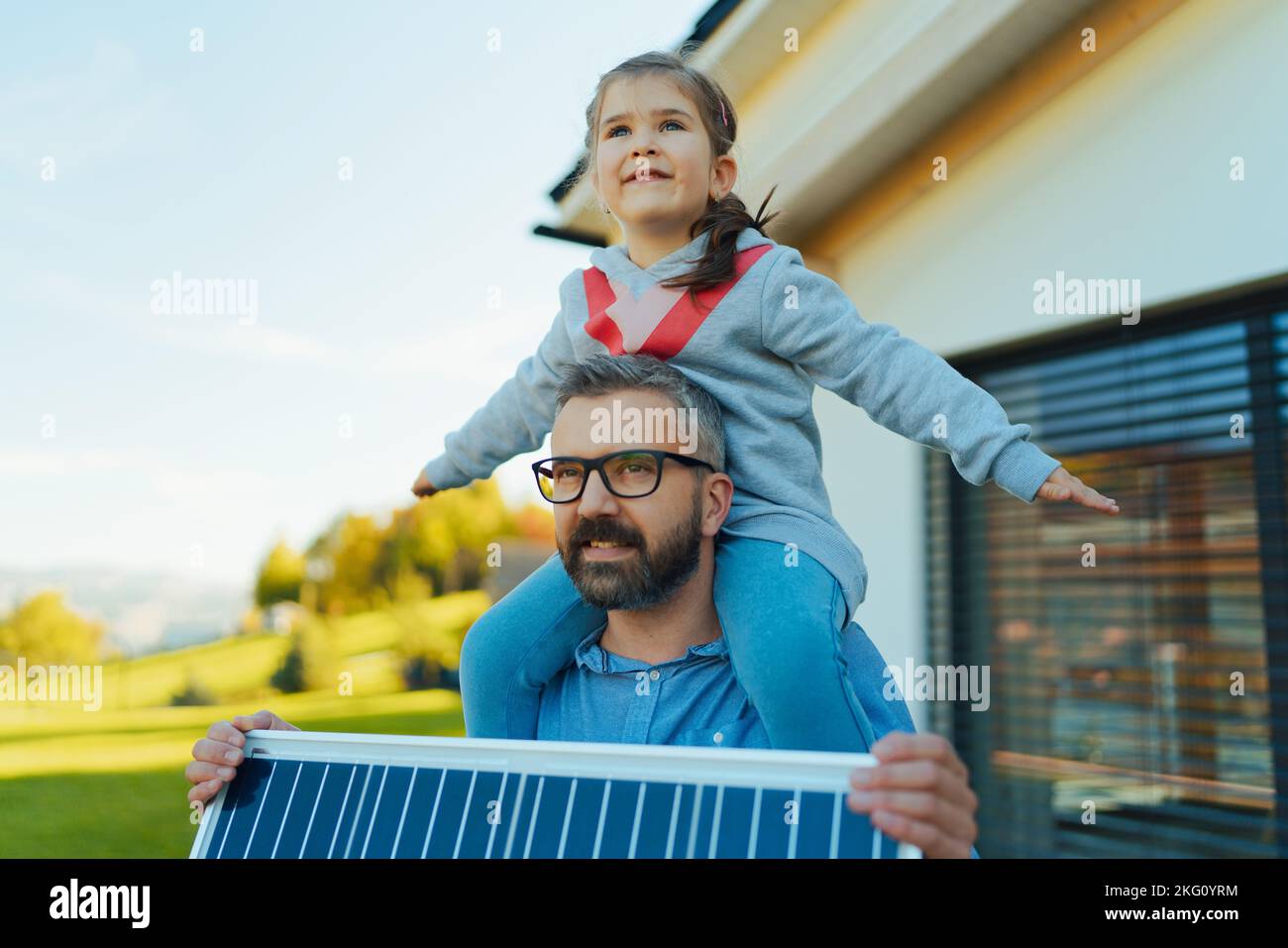 Father with his little daughter on piggyback, catching sun at solar ...