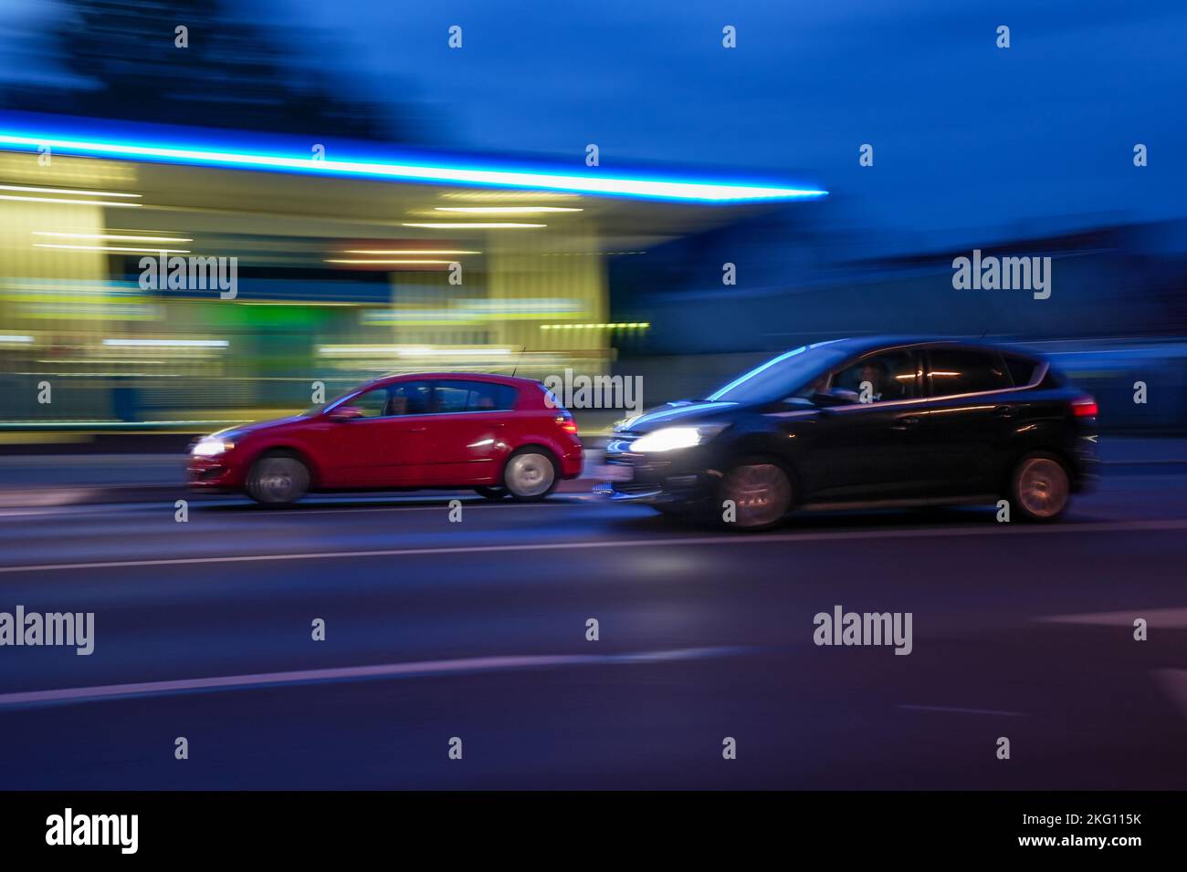 The fast-moving cars in the street at night with blurred gas station on ...