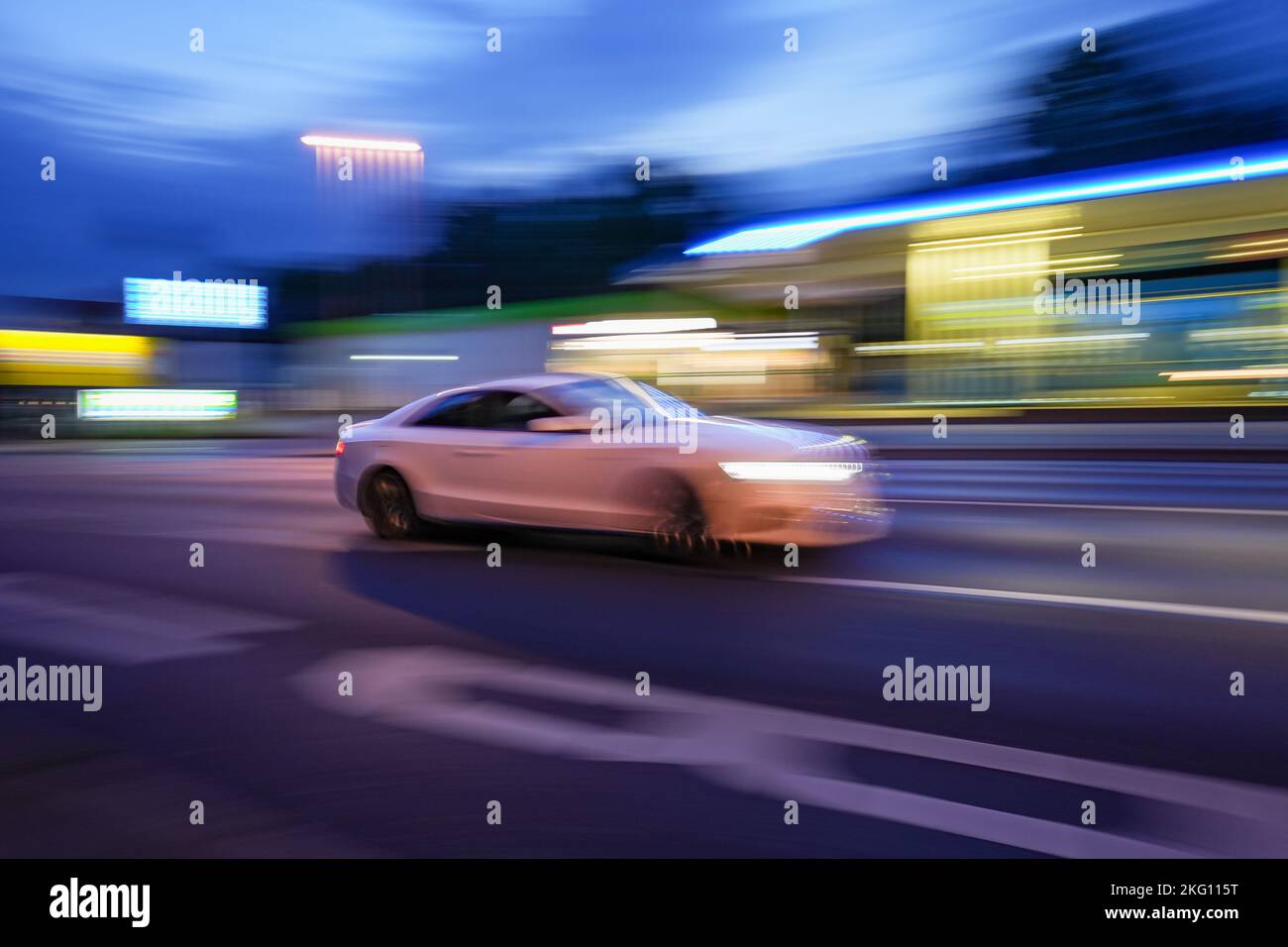 A fast-moving car in the street at night with blurred gas station on ...