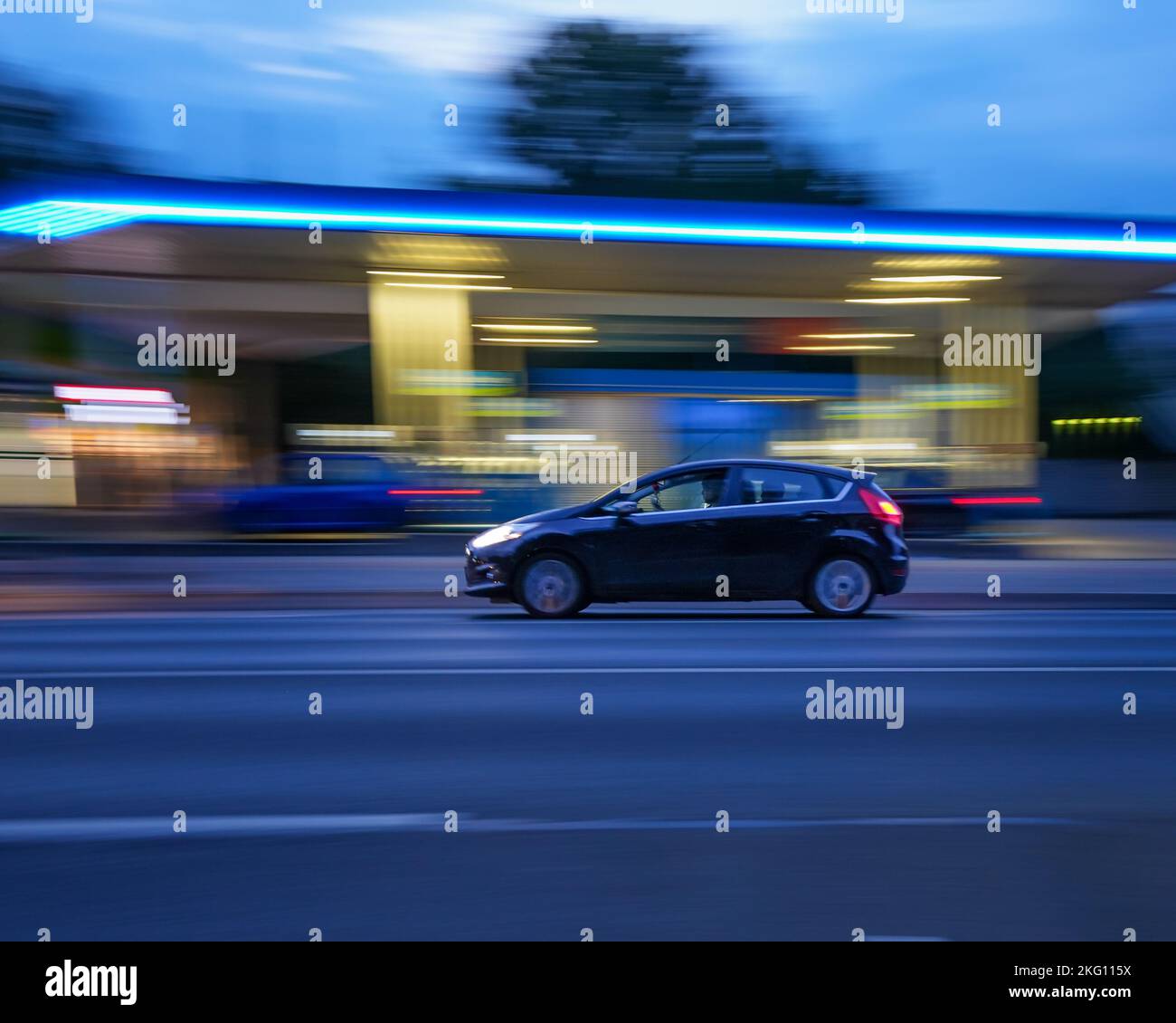 A fast-moving car in the street at night with blurred gas station on ...