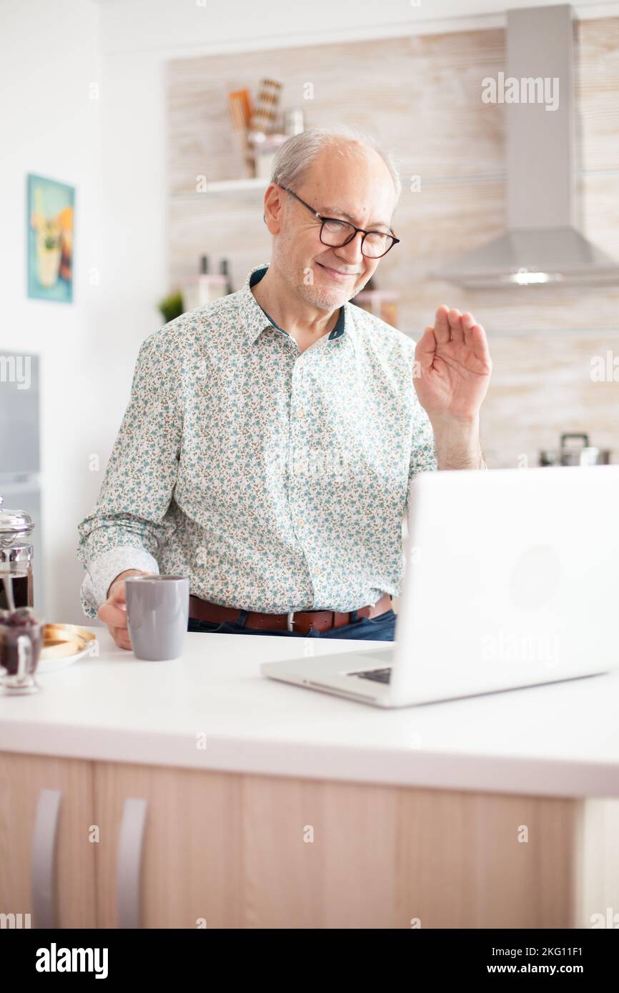 Old man saying hello during video call with family using notebook in ...