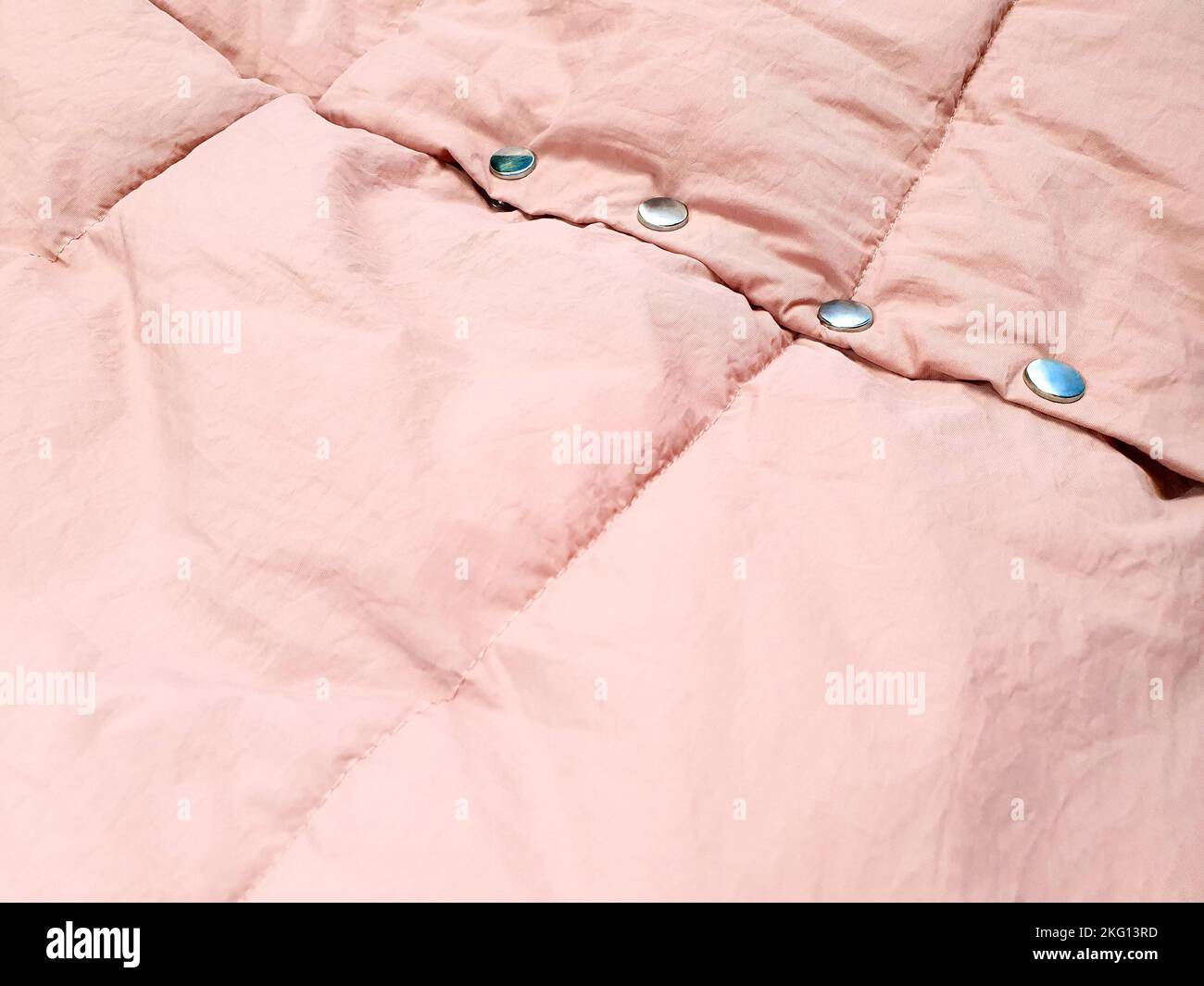 Down jacket fabric background and metal buttons or rivets, pink puffer ...