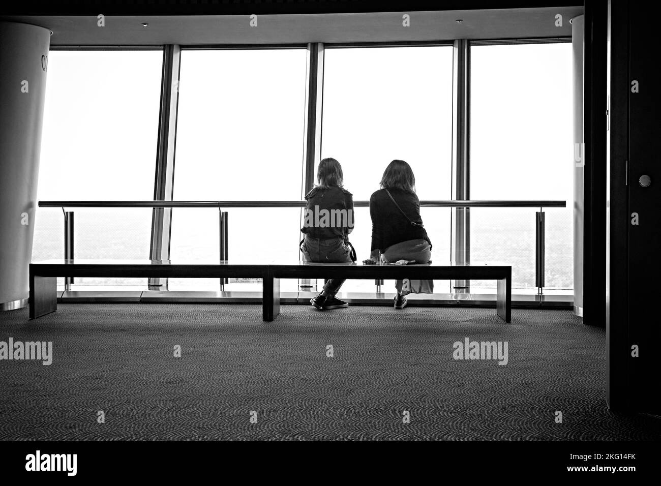 A black and white shot of two girls sitting on the bench facing the ...