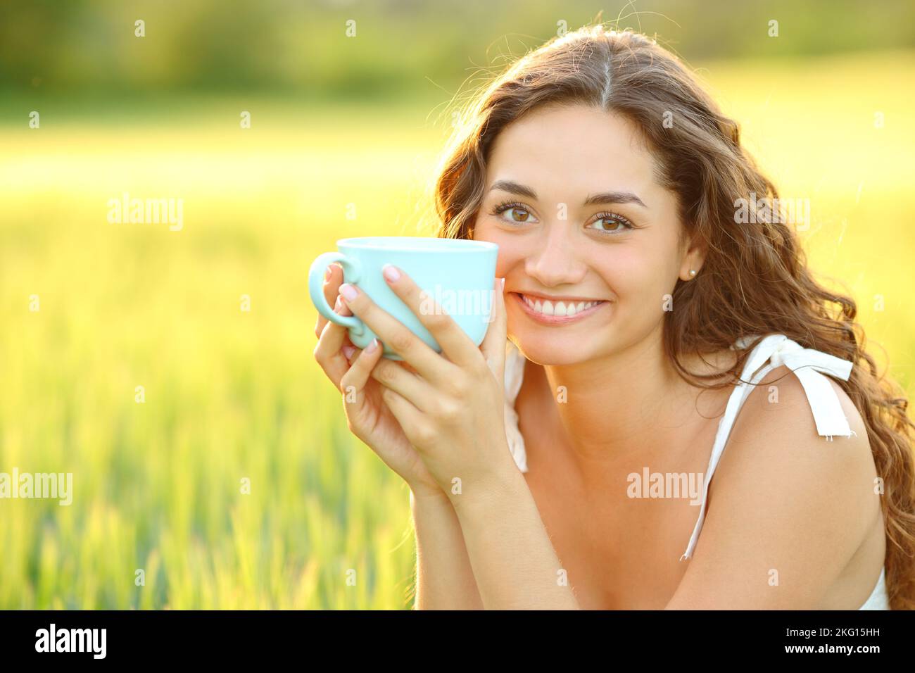 Happy beautiful woman holding coffee cup looking at camera in a wheat ...