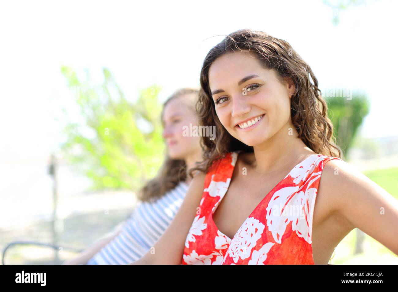 Happy woman with a friend looking at camera sitting in a bench Stock ...