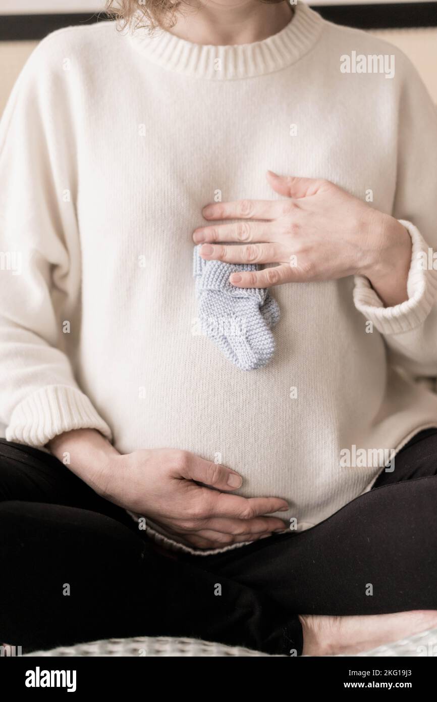 A pregnant woman in a warm knitted sweater and holding her belly. Soft ...