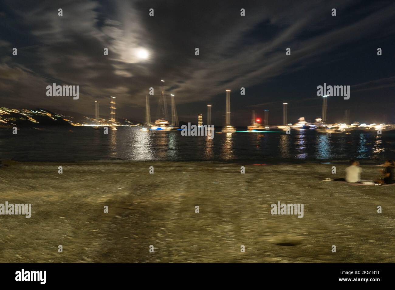 ICM. Couple sat on beach as the night is illuminated by the moon rising ...