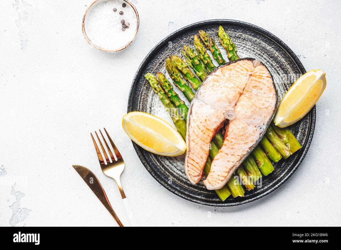 Baked steam salmon with asparagus and lemon on plate. White table ...