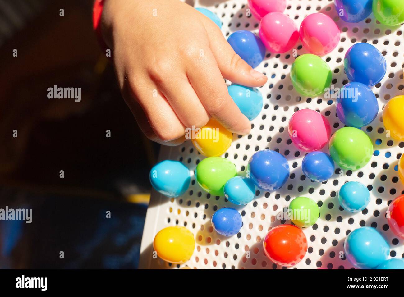Baby plays with colourful mosaics on white surface. Kids hand with ...