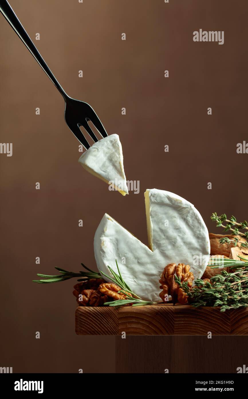 Brie cheese with walnuts, thyme, and rosemary on a brown background ...