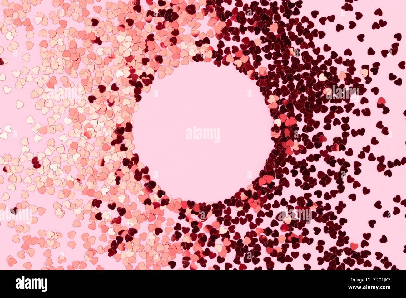 Round frame made of metallic red confetti in a heart shape on a pink ...