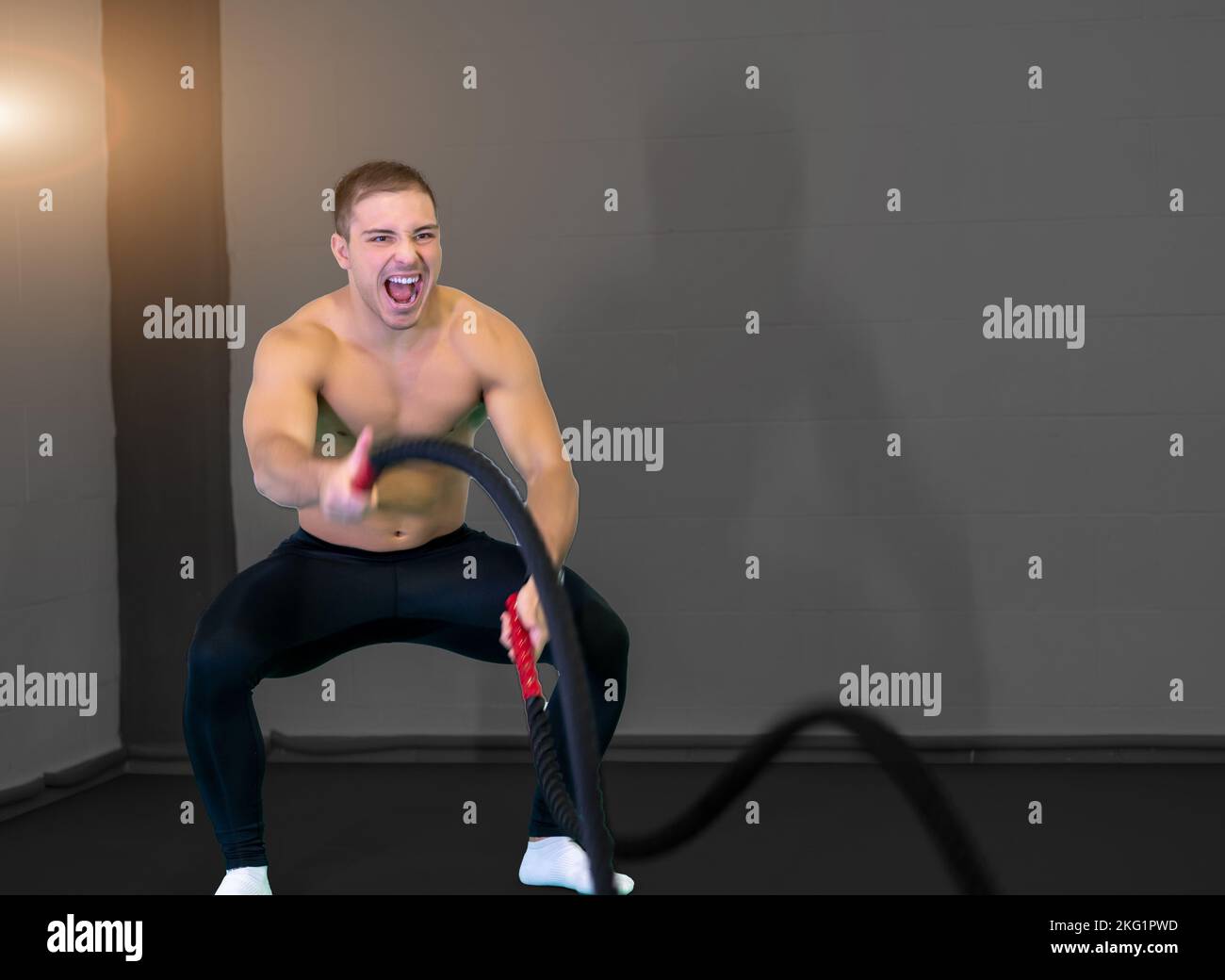 A handsome muscular young man using battle ropes for exercise in a gym ...