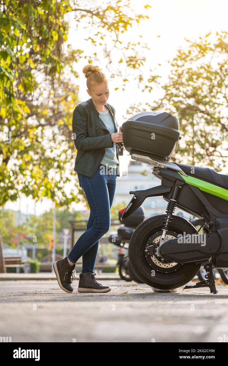 Red-haired woman opening the trunk of her parked motorcycle Stock Photo ...
