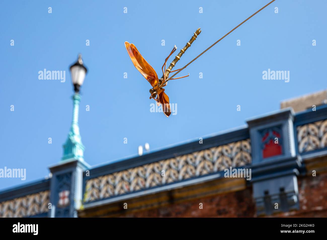 A Metal dragonfly on the background of the Tower of London, a moat part ...