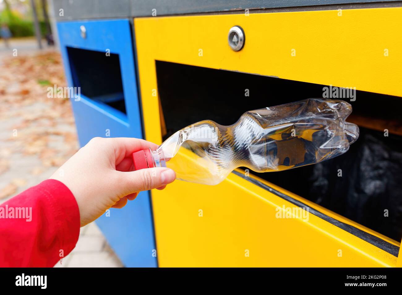 Hand throwing a plastic bottle into a colored garbage bin in the local ...