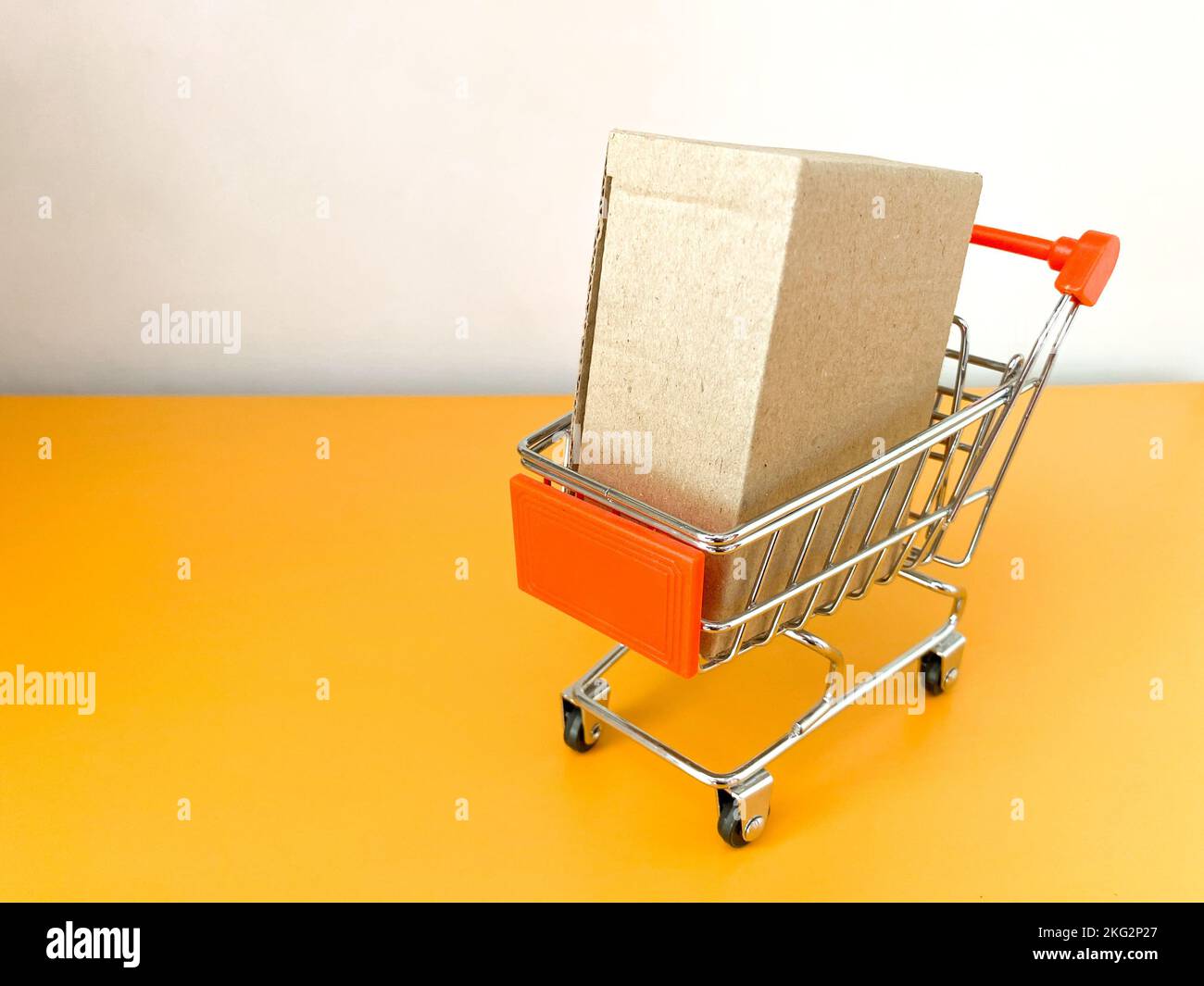 A mini shopping cart with a box on an orange surface Stock Photo - Alamy