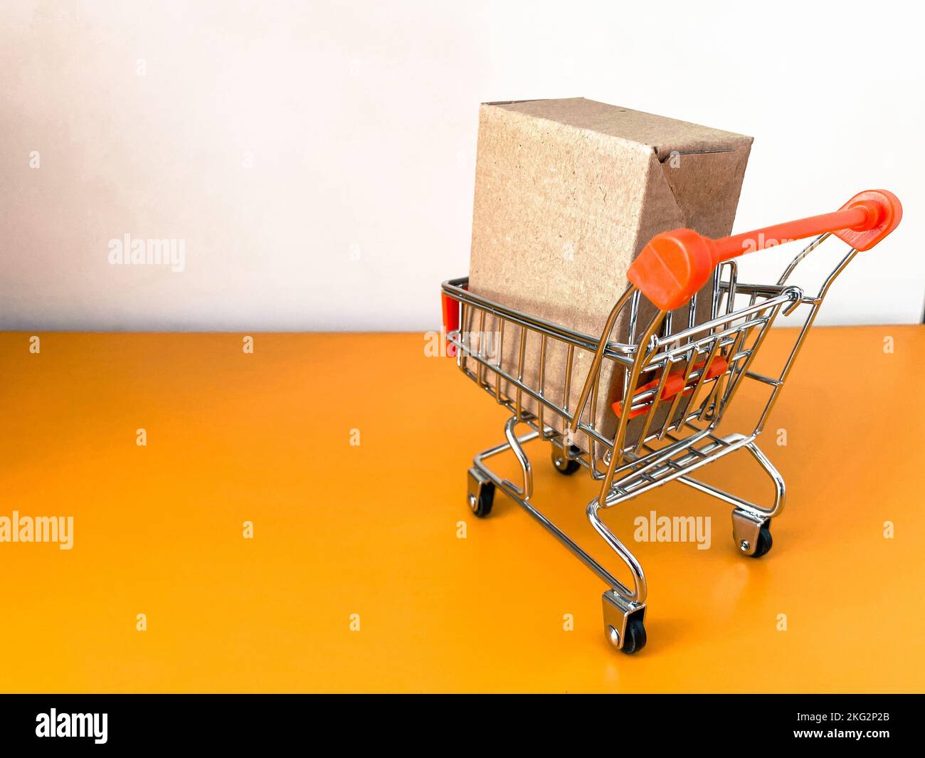 A mini shopping cart with a box on an orange surface Stock Photo - Alamy
