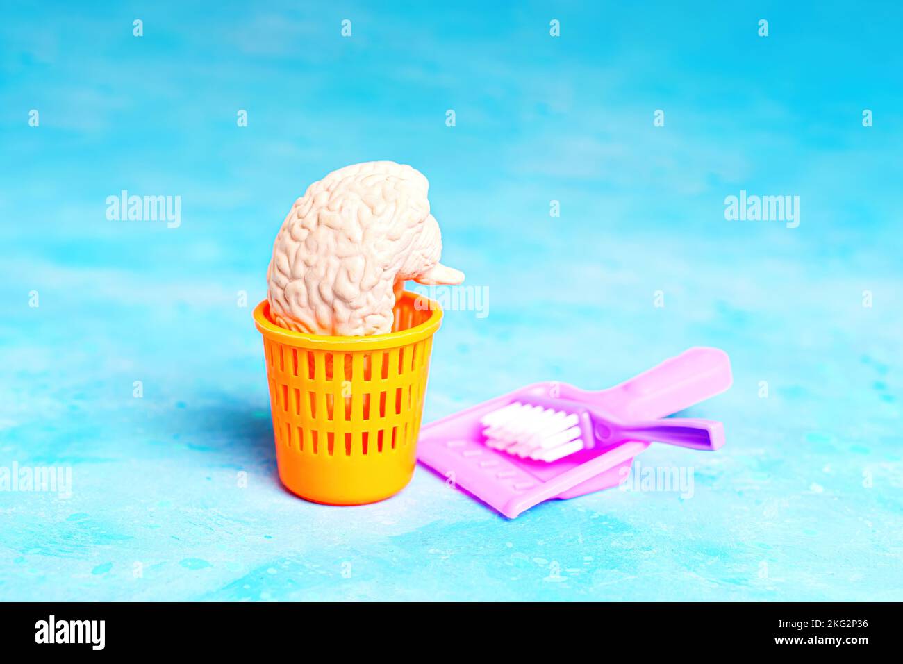 Human brain in a trash bin and toy home cleaning tools arranged on blue ...